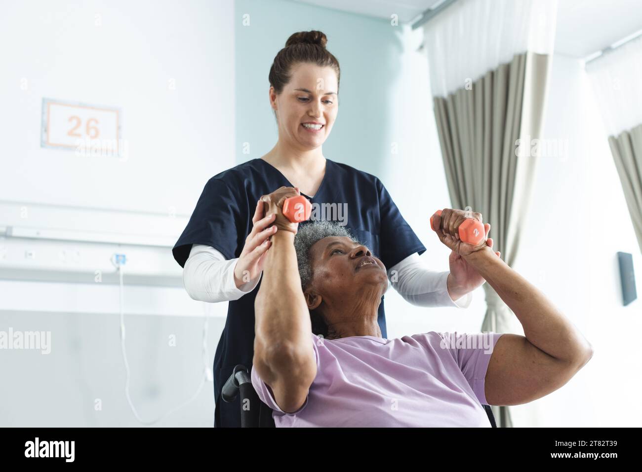 Diverse senior female patient exercising with weights and female doctor ...
