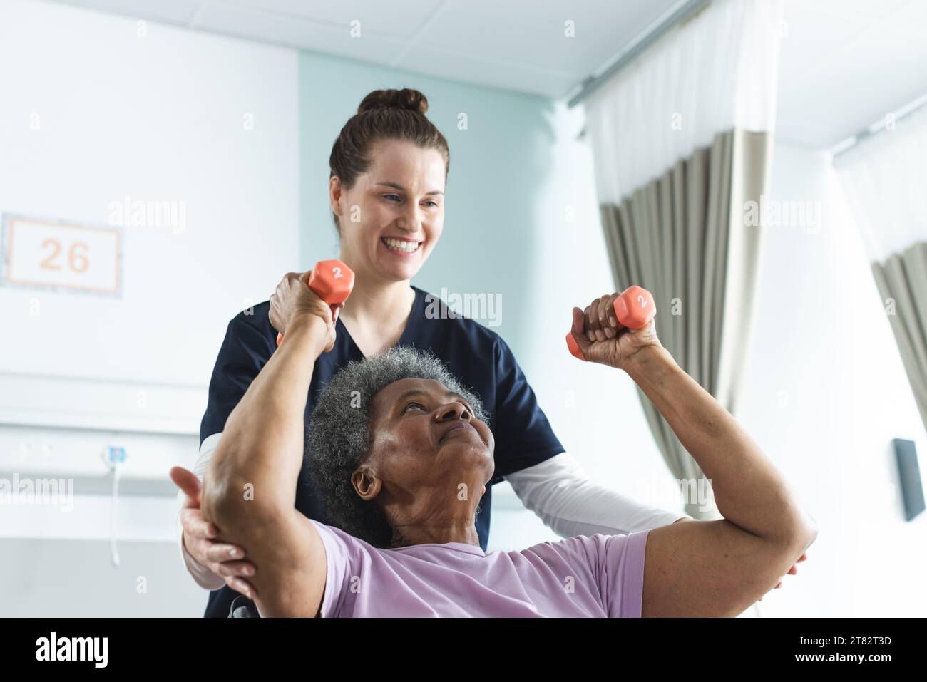 Diverse senior female patient exercising with weights and female doctor ...