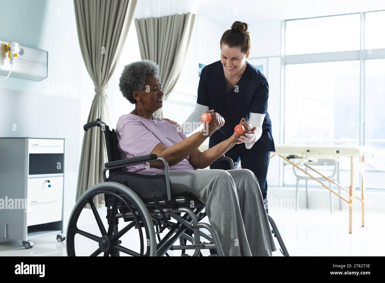 Diverse senior female patient exercising with weights and female doctor ...