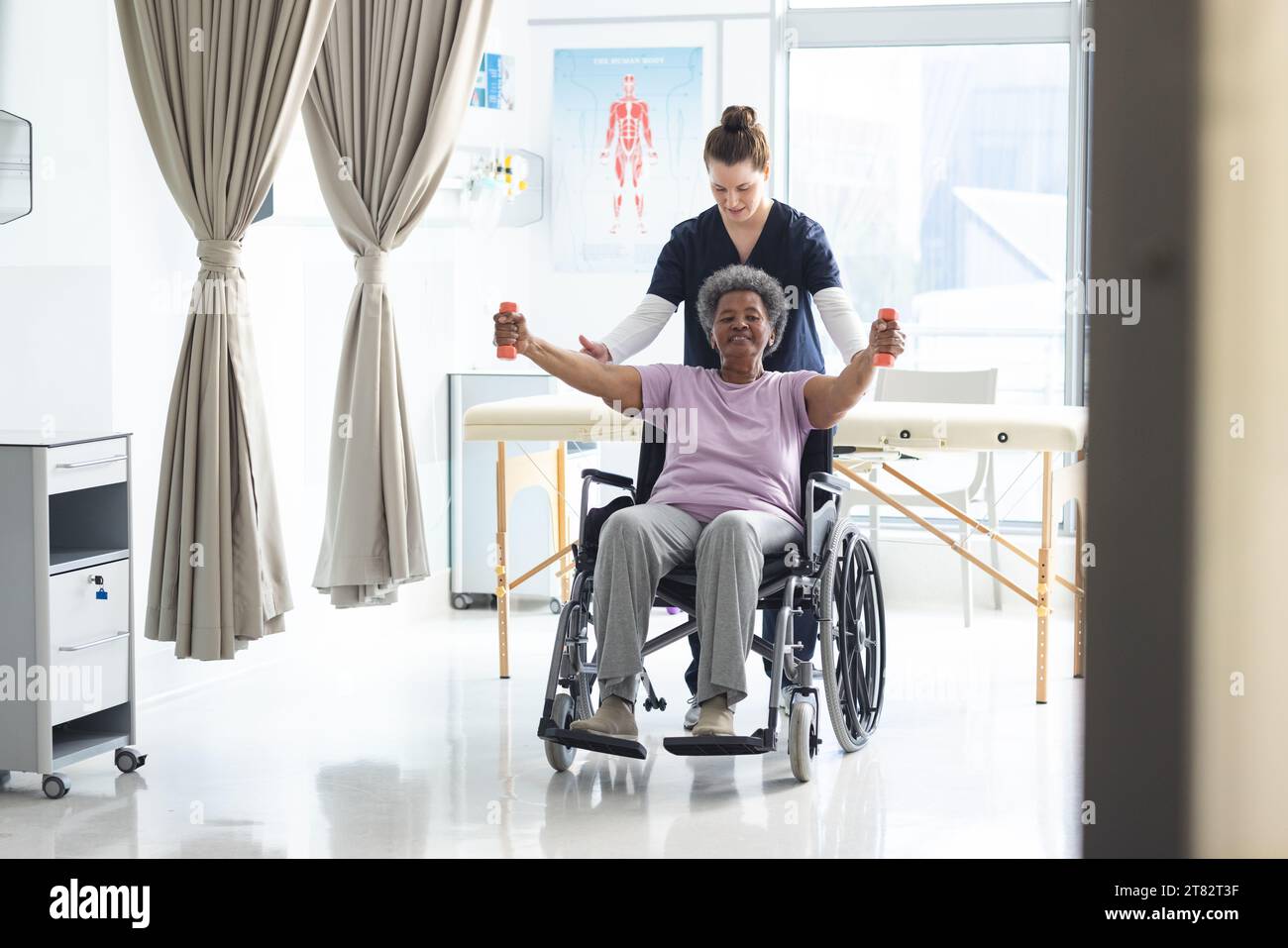 Diverse senior female patient exercising with weights and female doctor ...