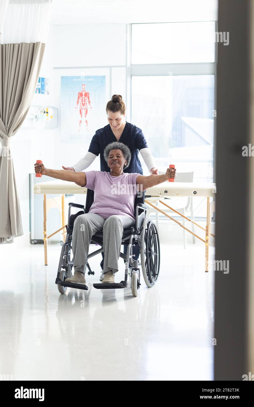 Diverse senior female patient exercising with weights and female doctor ...