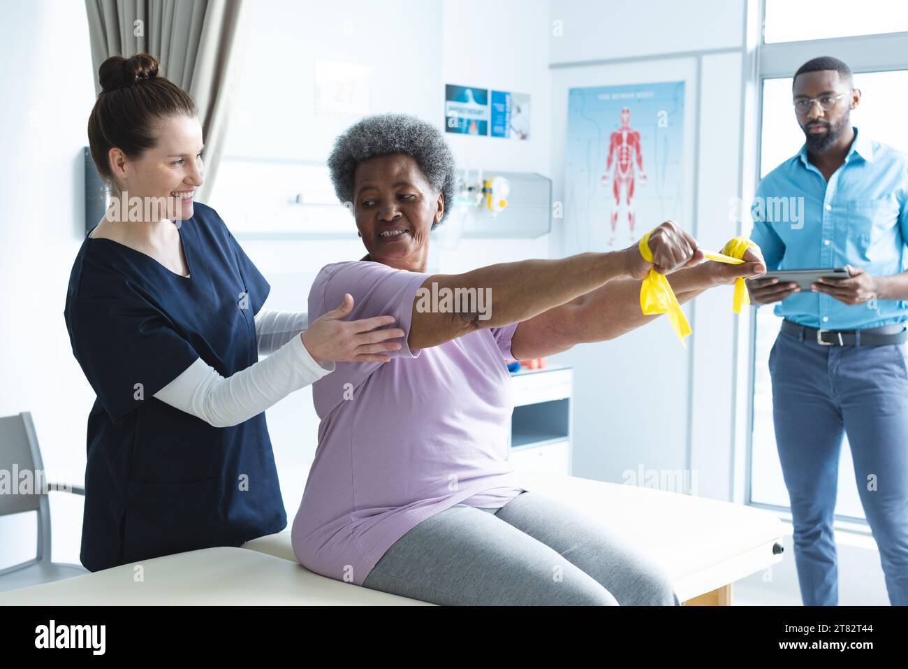 Diverse senior female patient exercising with band and female doctor ...