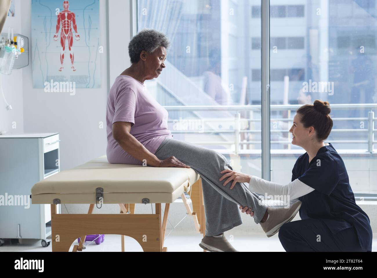 Diverse senior female patient exercising leg and female doctor advising ...