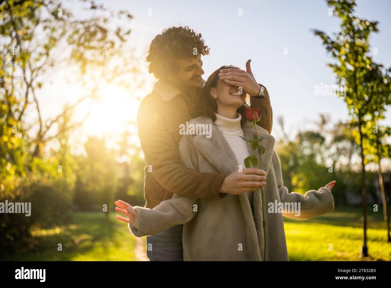 Portrait of happy loving couple in park in sunset. Man is giving rose ...