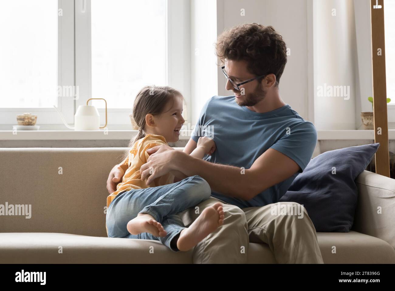 Playful girl tickling father sitting on couch Stock Photo - Alamy