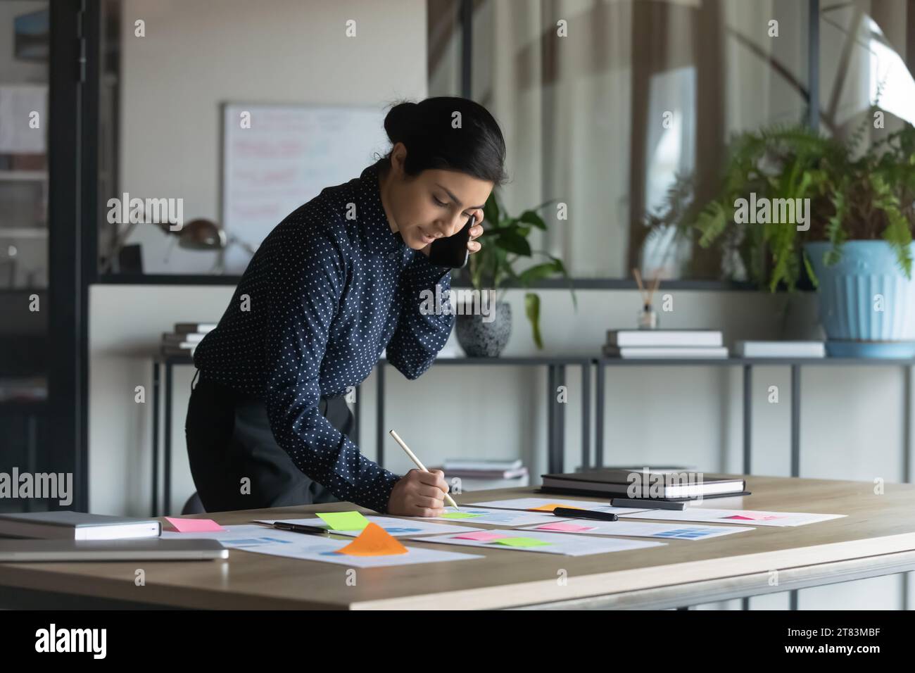 Serious busy multitasking young Indian businesswoman working with ...