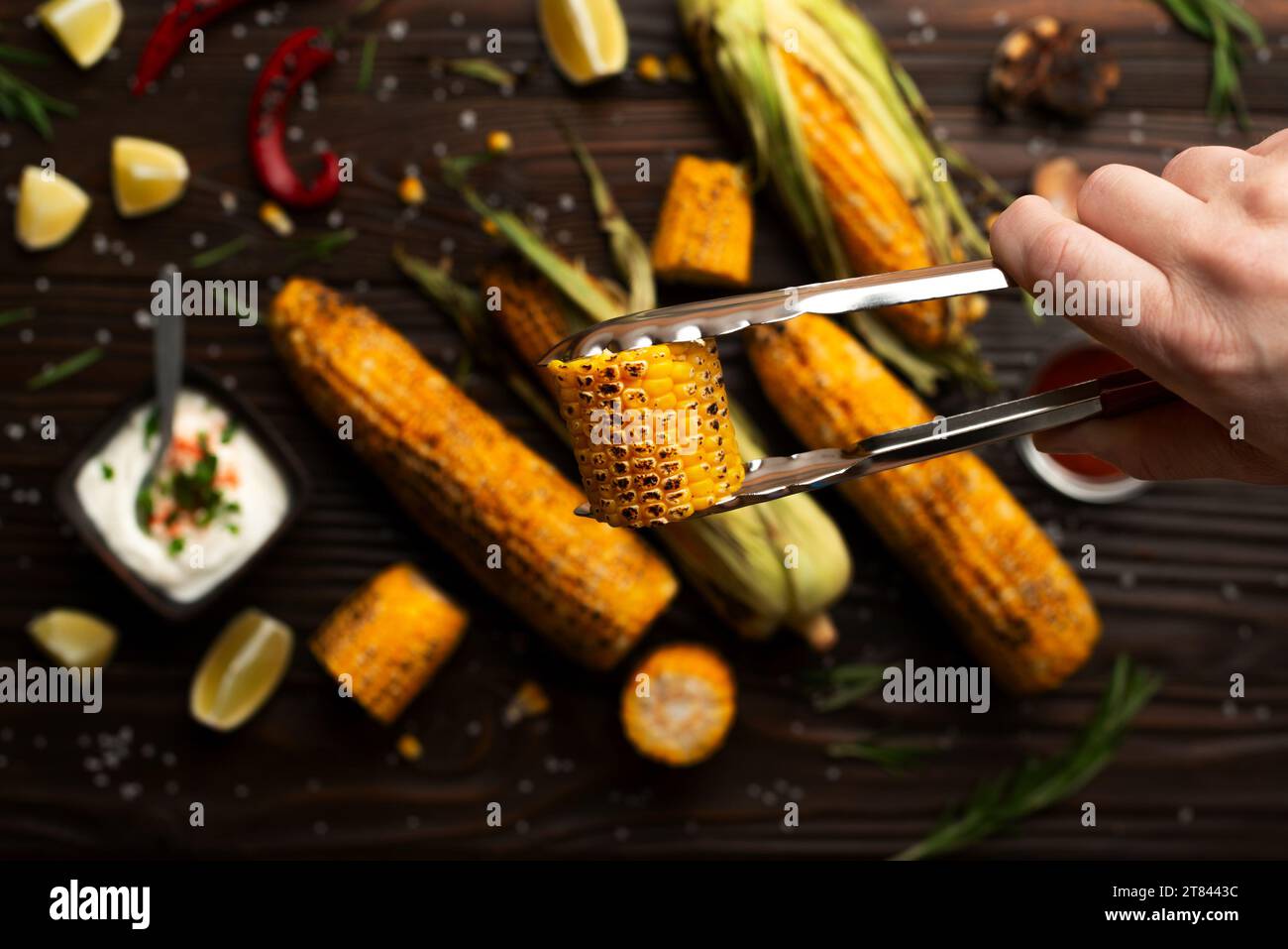 Kitchen tongs with grilled corn on the cob pieces in caucasian hands on ...
