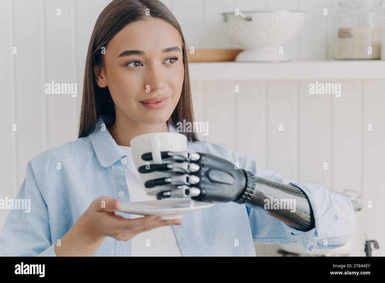 A young woman with a bionic prosthetic hand admiringly holds a cup, a ...