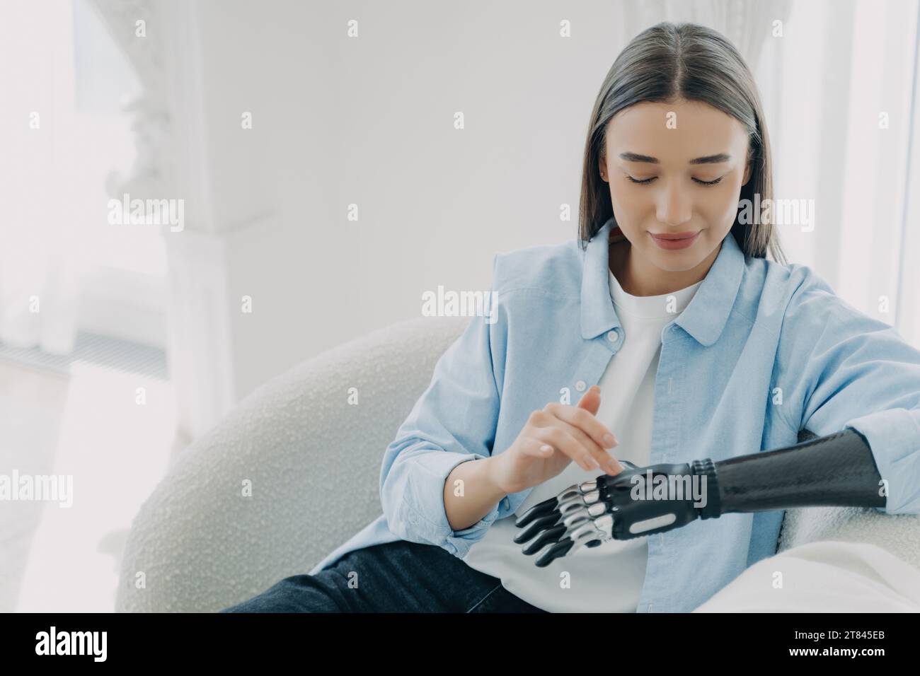 Content woman with bionic hand gently touching her forearm, showcasing ...