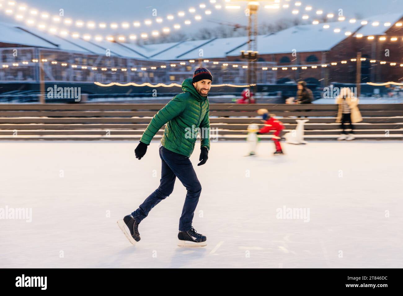Man ice-skating joyfully in an outdoor rink with festive lights at ...