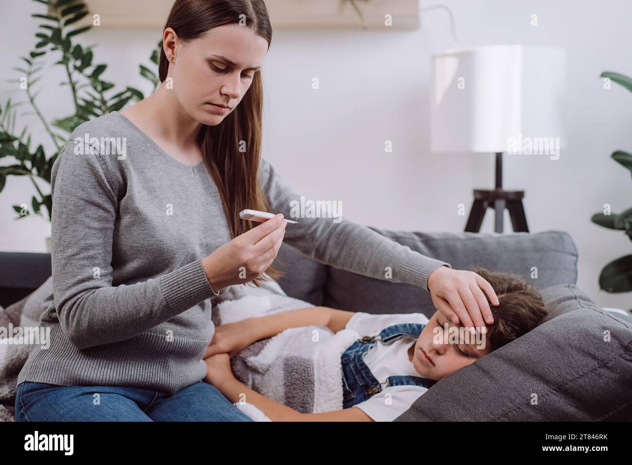 Worried young caucasian mother treating sick daughter kid suffering from flu and fever, holding ...