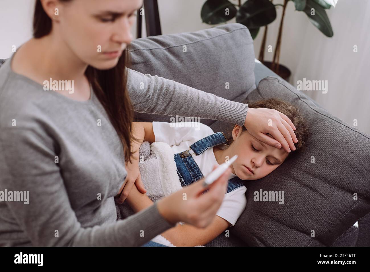 Selective focus of caring young mother checking high body temperature of ill daughter, touching ...