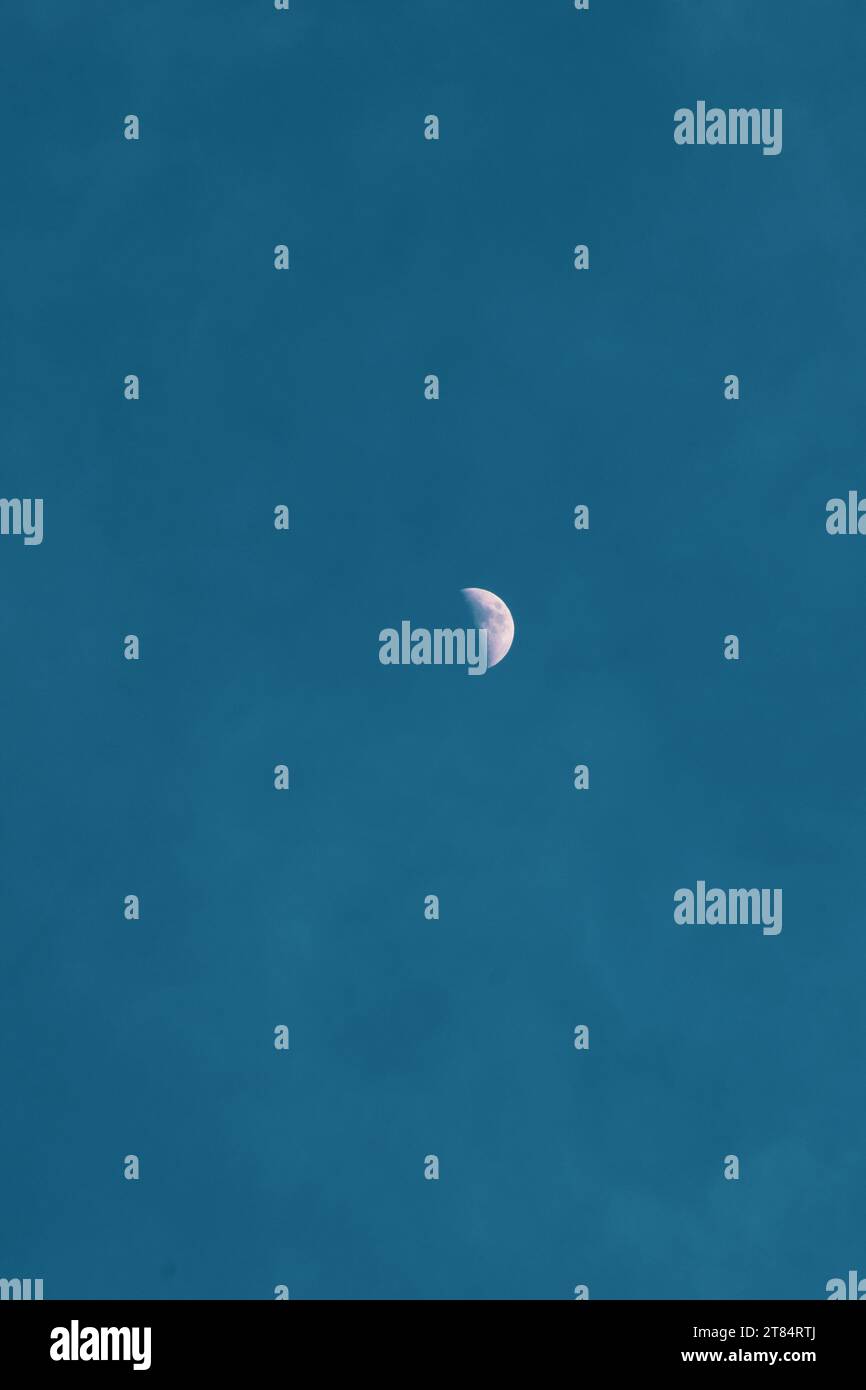 Half of the moon. The lunar surface is visible. Clear blue sky in the ...