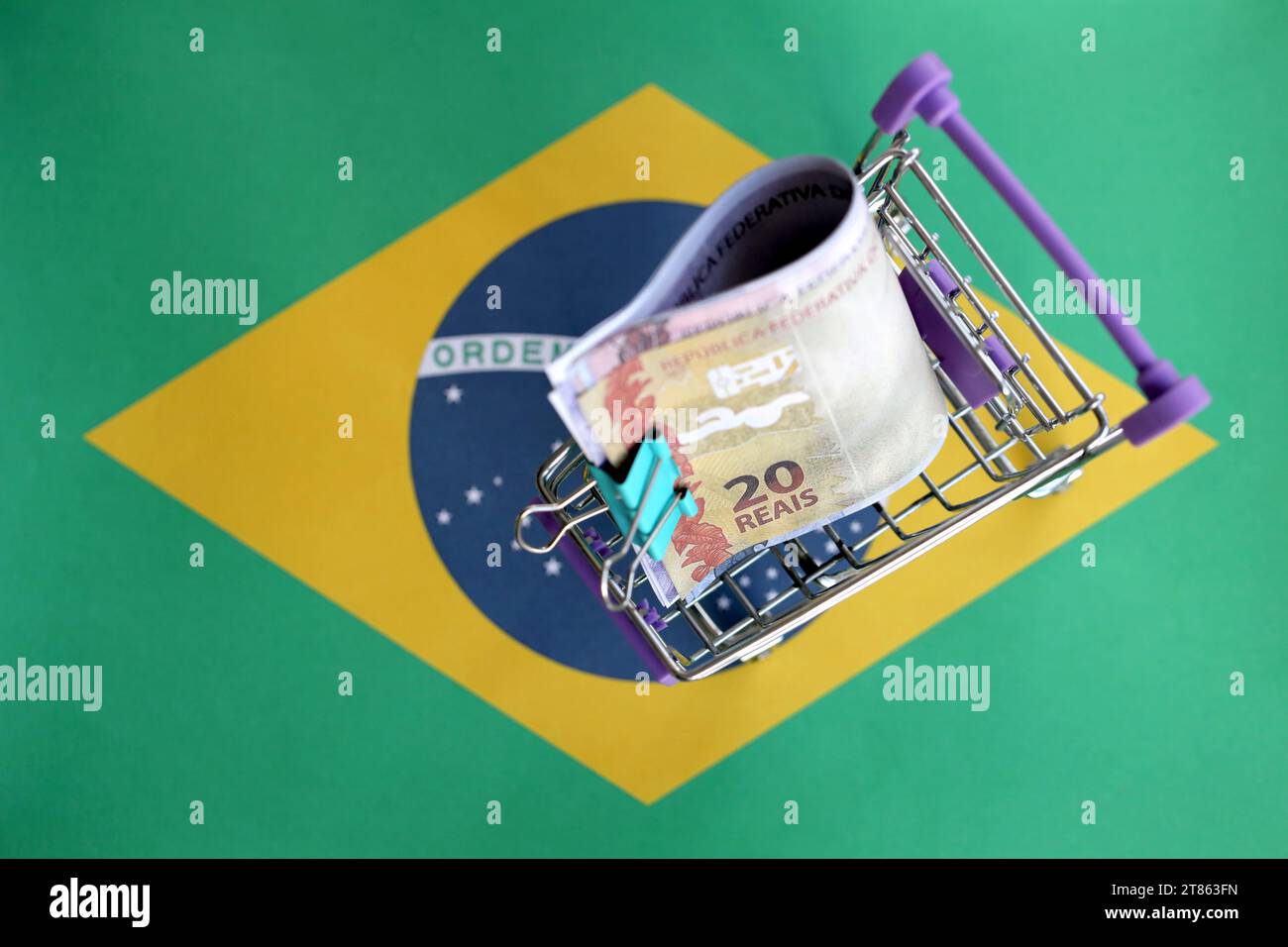 Brazilian money bills in small shopping cart close up on Brazilian flag ...