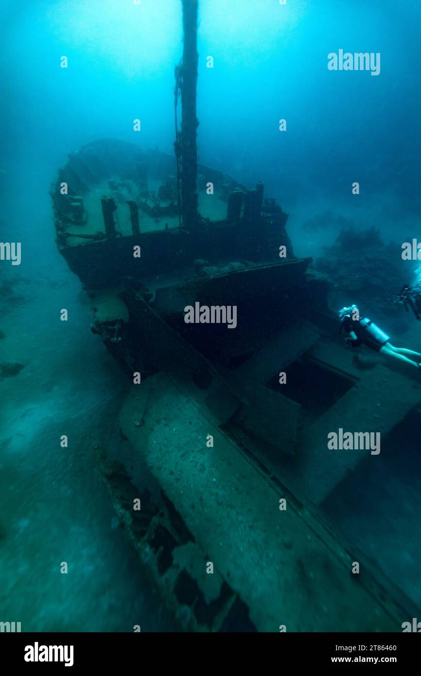 Scuba divers pass over sunken shipwreck of an old cargo ship in clear ...