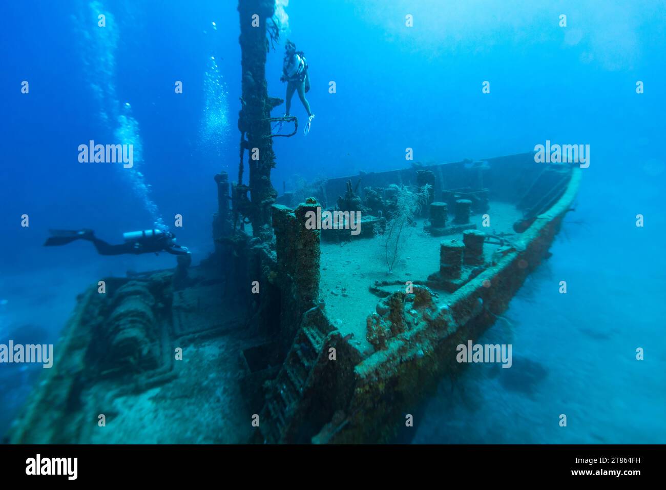 Scuba divers pass over sunken shipwreck of an old cargo ship in clear ...