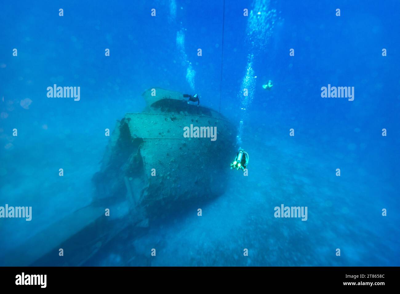 Scuba divers pass over sunken shipwreck of an old cargo ship in clear ...