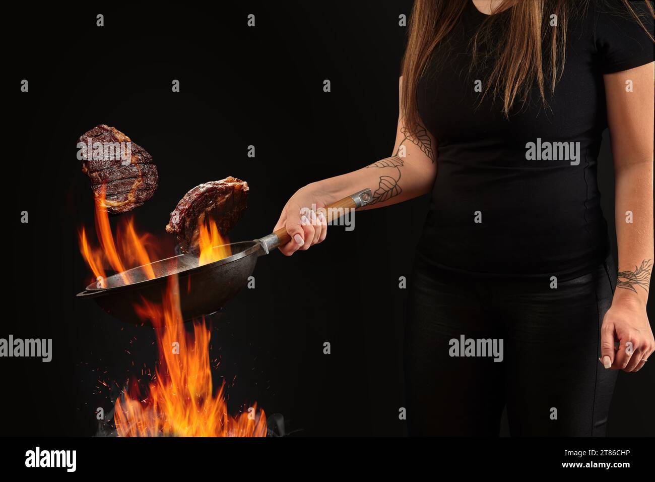Cook with tattooed hands, dressed in leggings and t-shirt. Holding wok ...