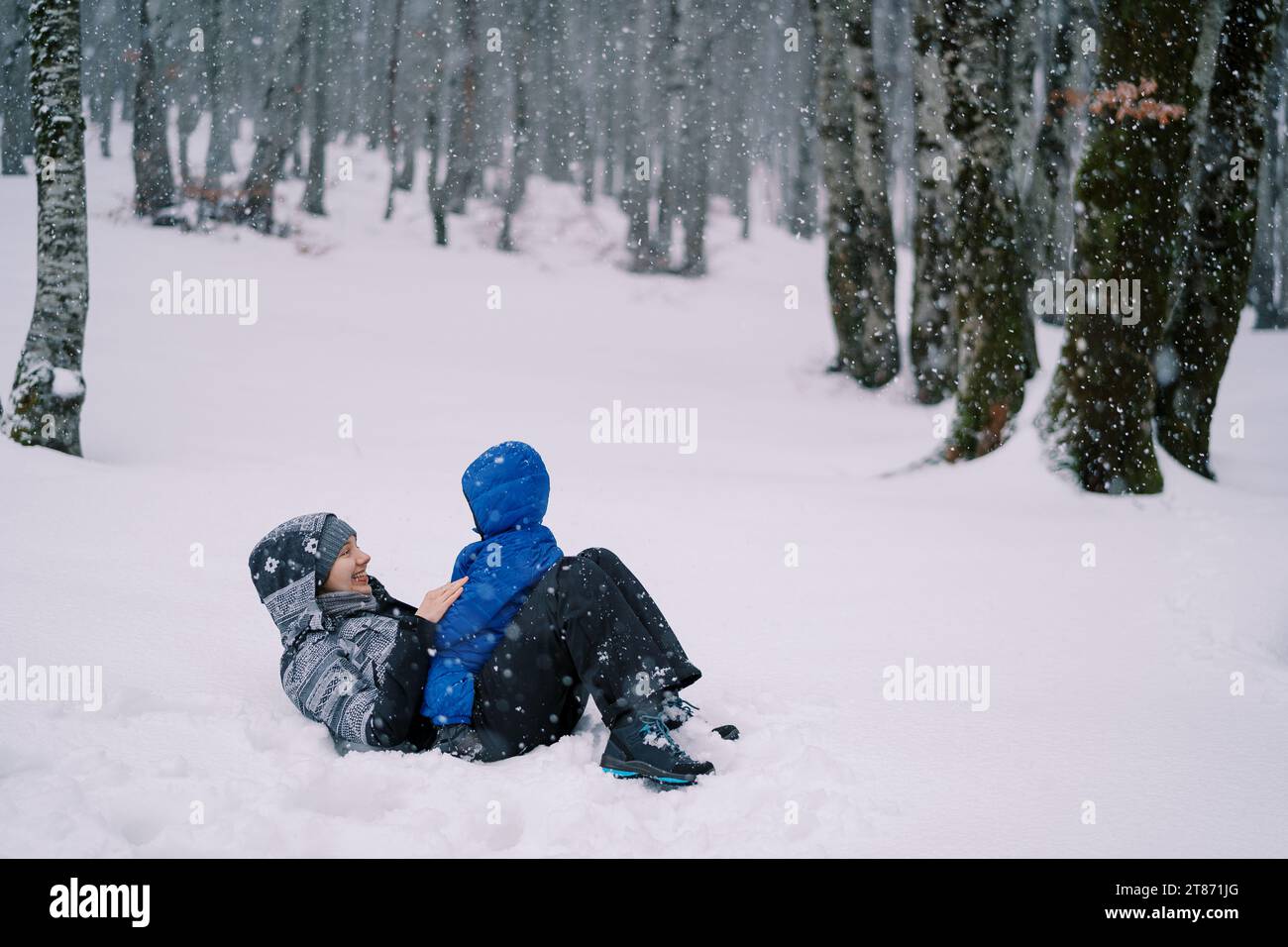 Mom with a small child on her stomach lies in a snowdrift in a winter ...