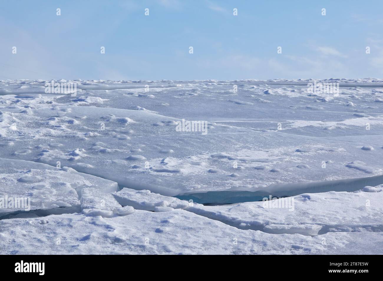 Winter ice landscape under blue sky and clouds. Cracks in the ice field ...