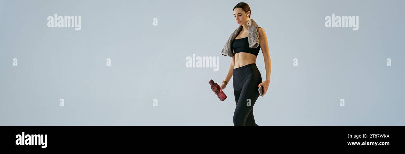 Woman walking with water bottle and towel around her neck over studio ...