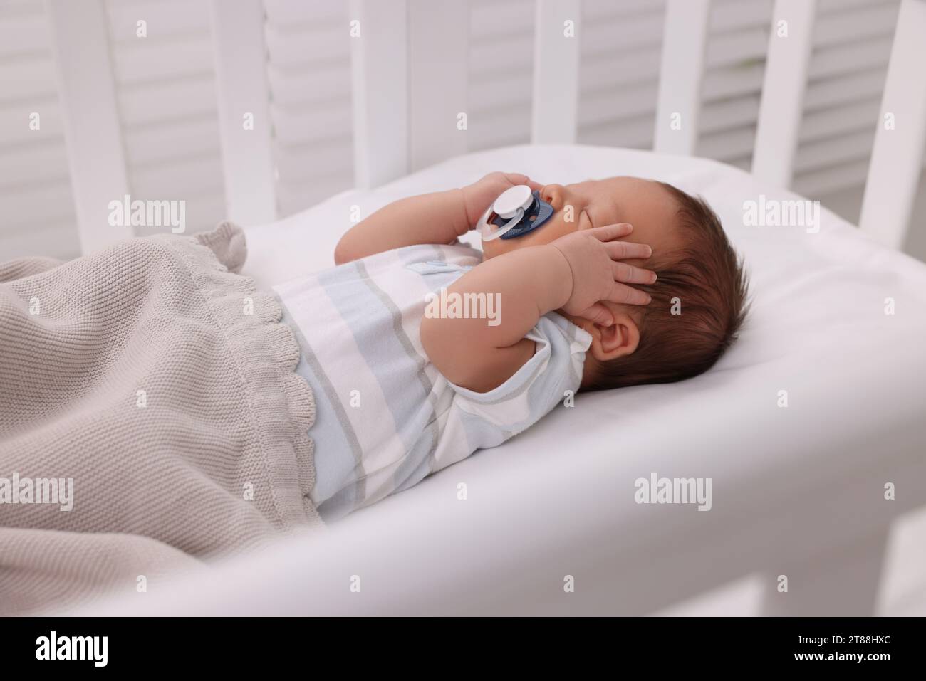 Cute newborn baby with pacifier sleeping under blanket in crib. Bedtime ...