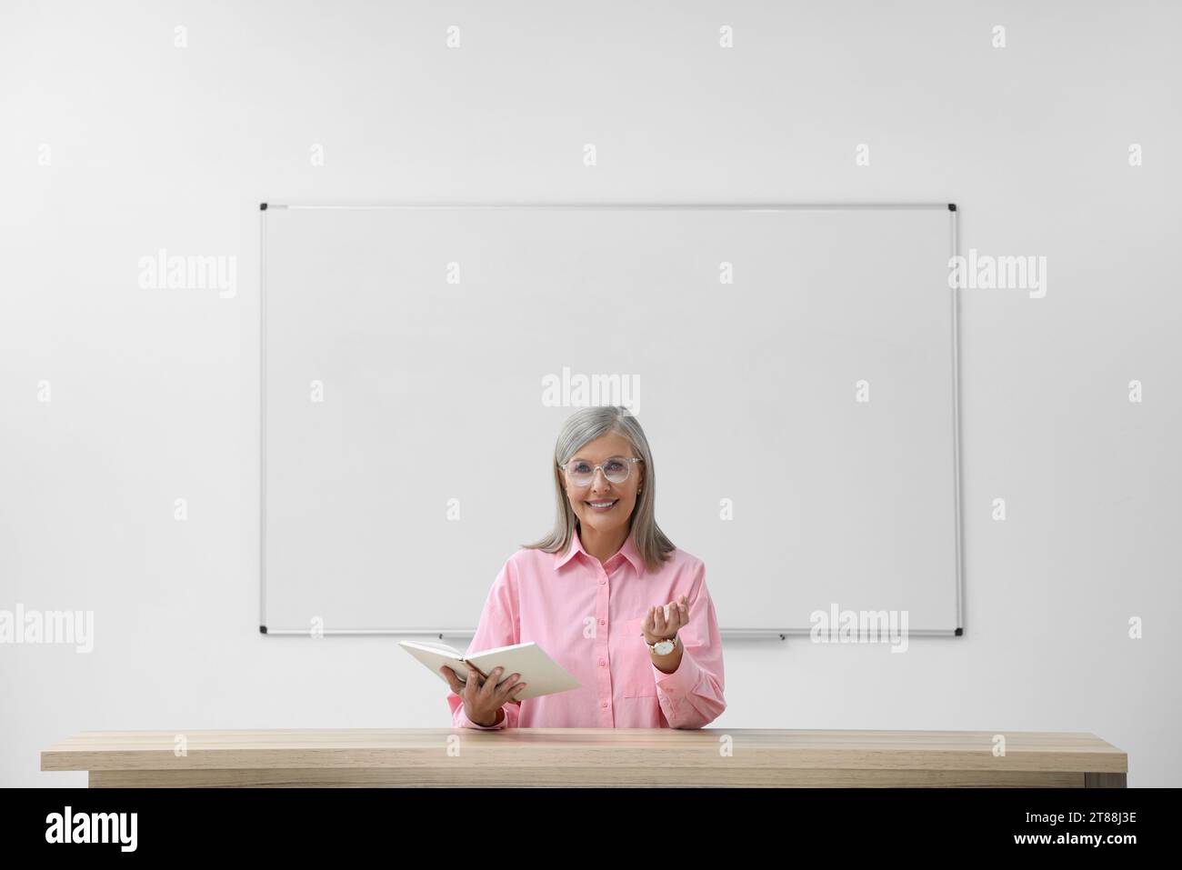 Happy professor with book giving lecture at desk in classroom Stock ...