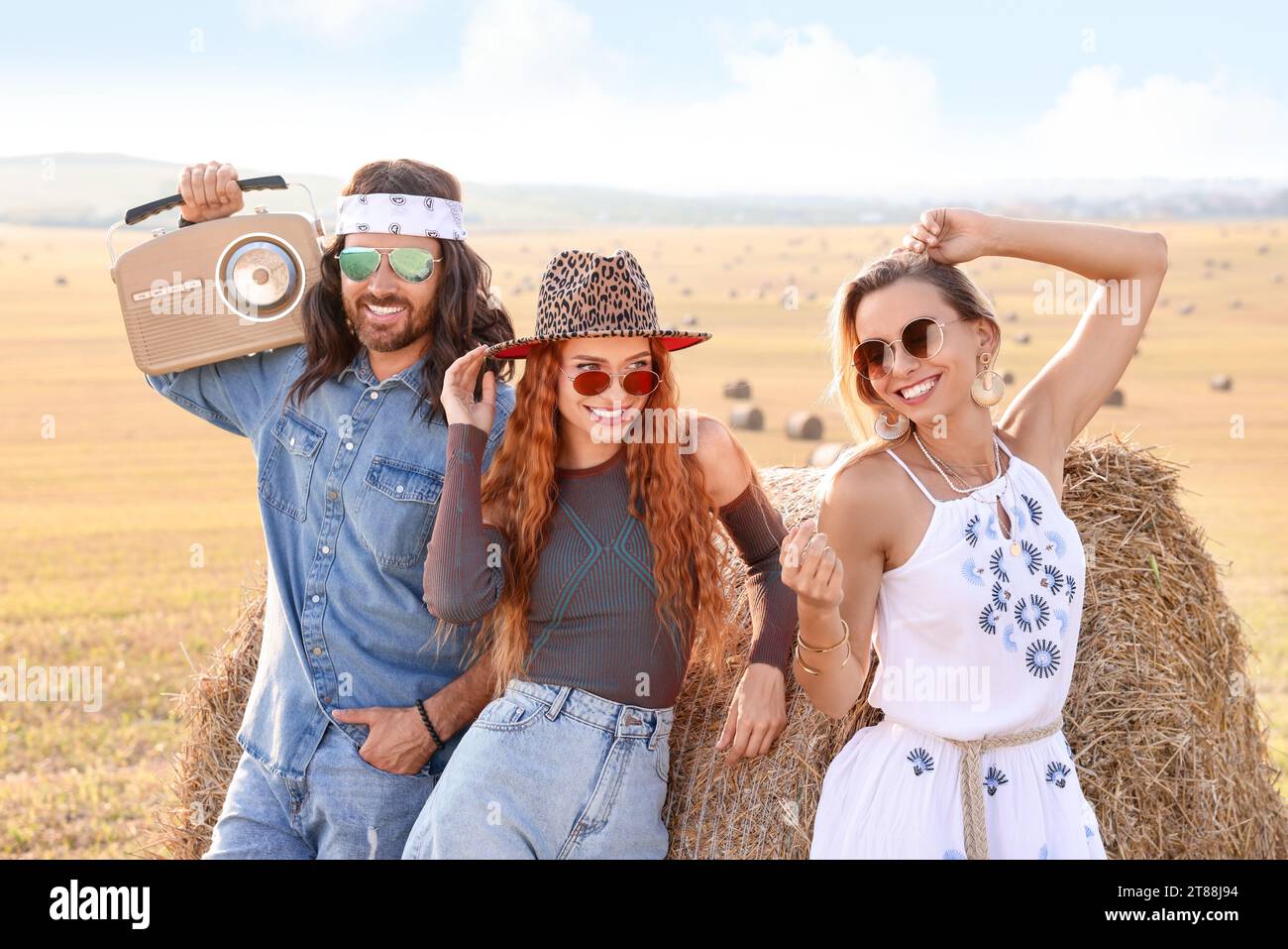 Happy hippie friends with radio receiver near hay bale in field Stock ...