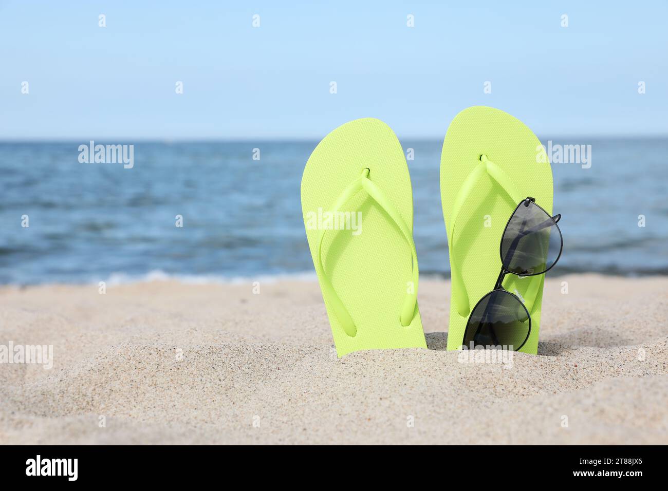 Stylish light green flip flops and sunglasses on beach sand, space for ...