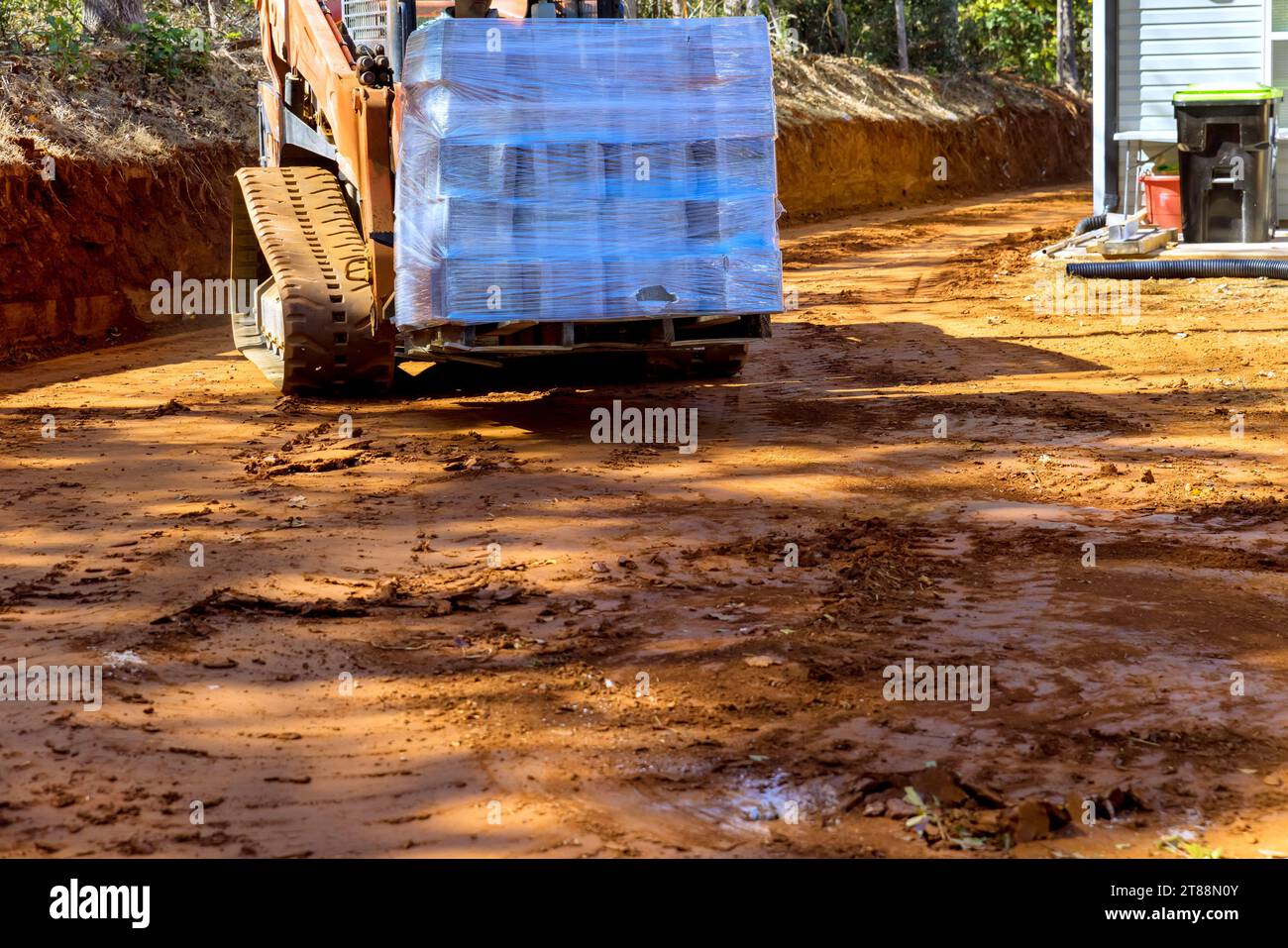 As worker works with small forklift he is unloading pallets of concrete ...