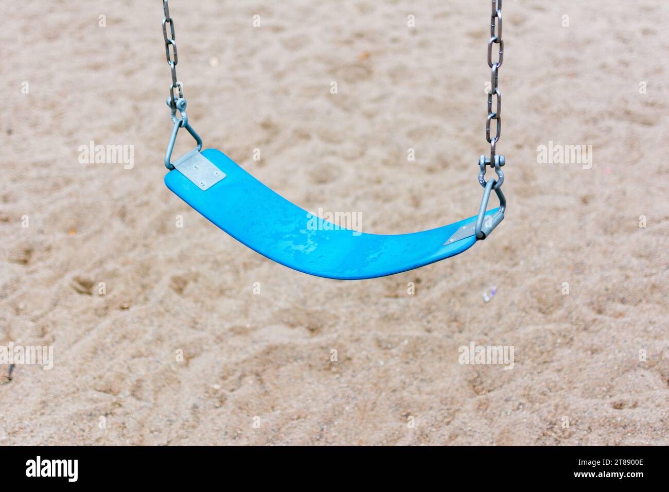 A single blue swing with chain links suspended over a sea of sand on a ...