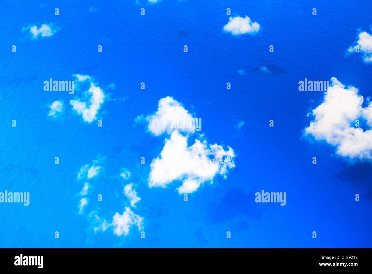 Puffy white clouds move across a deep blue ocean, their shadows cast ...