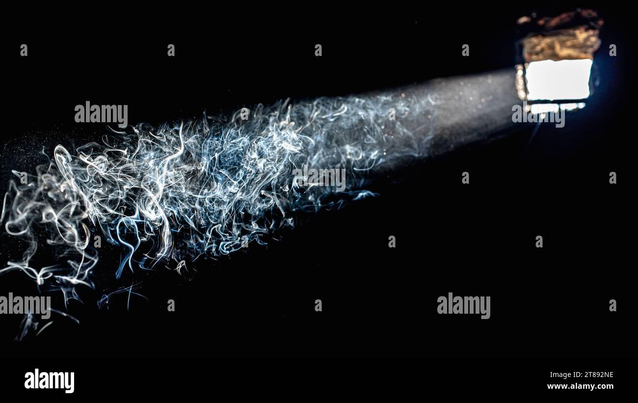 Puffs of cigarette smoke in a dark room, illuminated by a ray of light ...