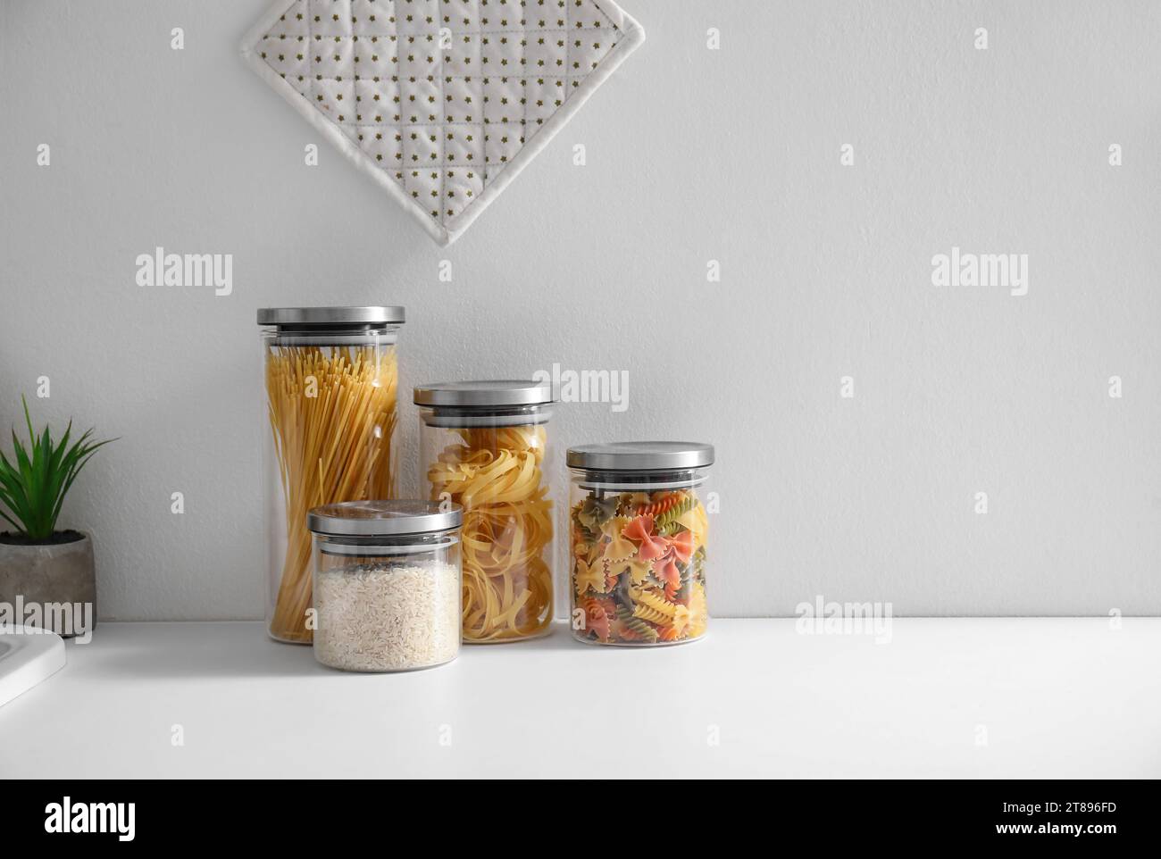 Glass jars with different types of pasta on white counter in kitchen ...