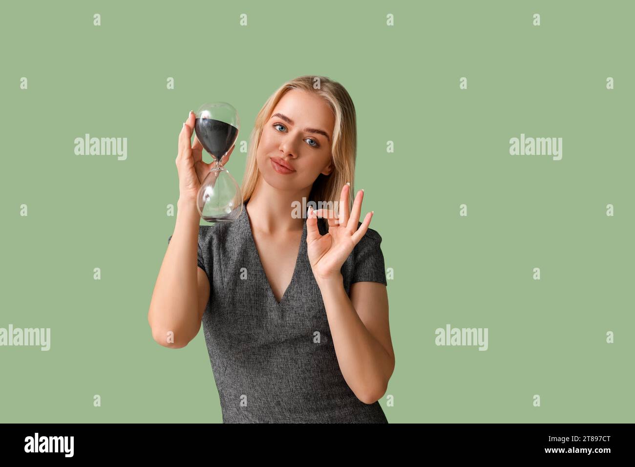 Young happy businesswoman with hourglass showing OK gesture on green ...