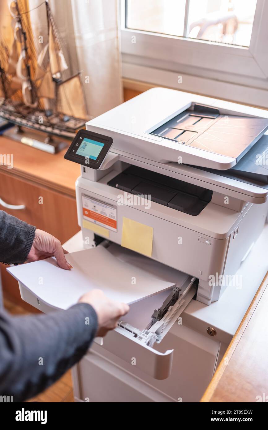 Woman putting paper in a printer to make photocopies and teleworking ...