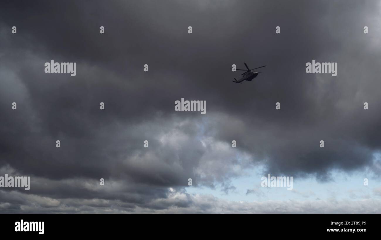Black stormy sky covered with dark rain clouds with a flying helicopter ...