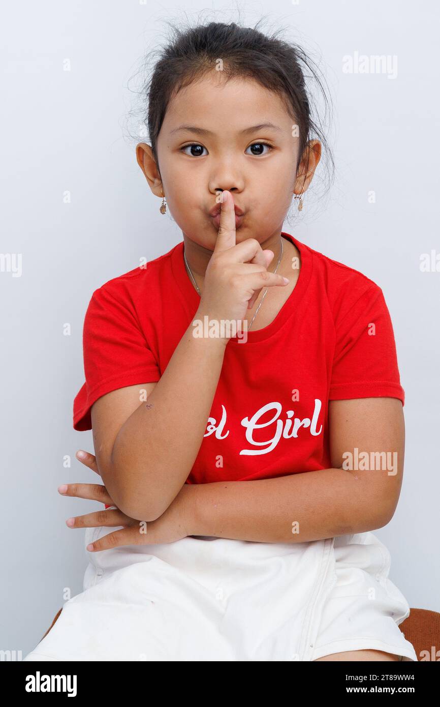Portrait of a cute little asian girl making silence gesture on white ...