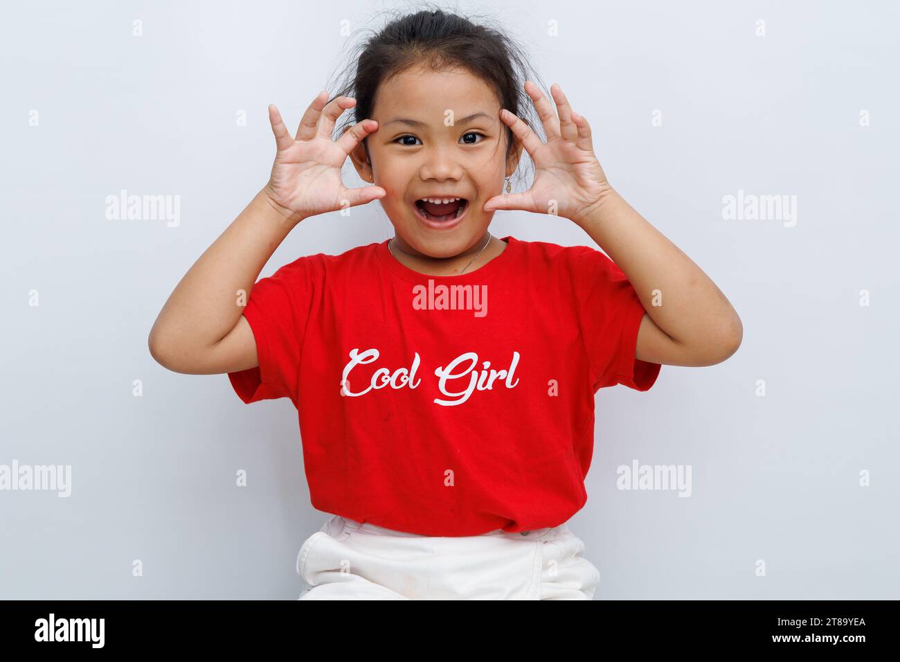Little Asian girl raises both hands parallel to her head making a ...