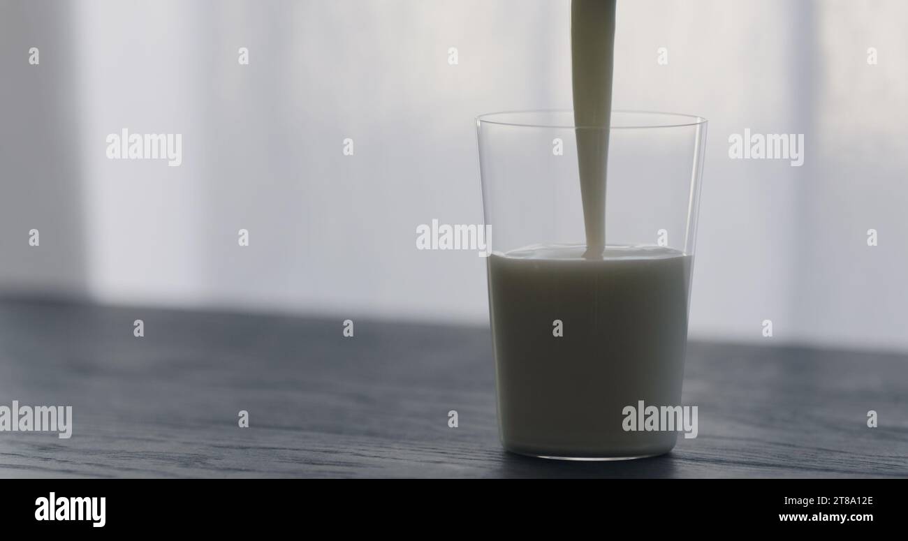pour organic yogurt in tumbler glass on black wood table with copy ...