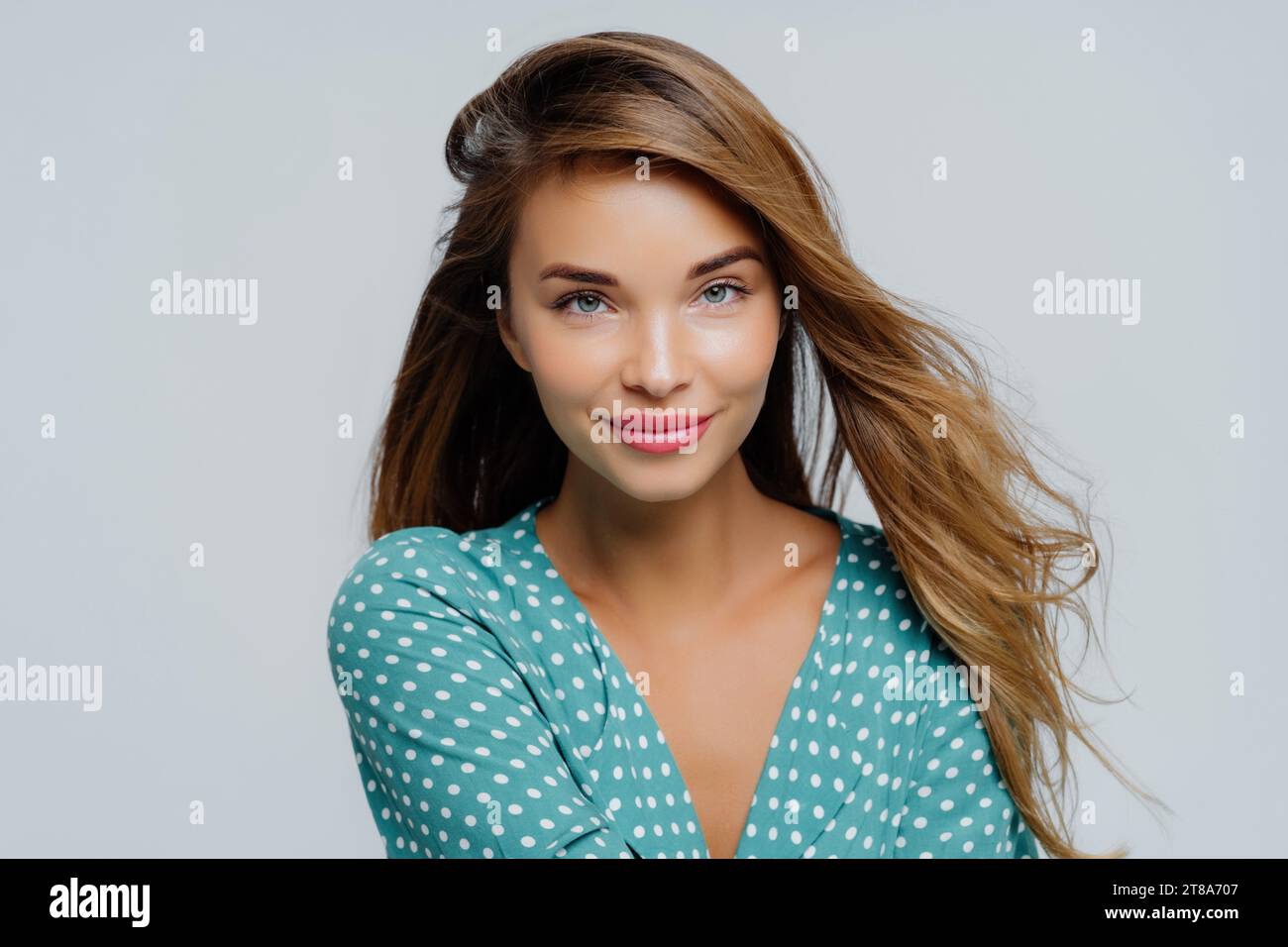 Charming woman with flowing hair in a polka dot dress posing on a ...