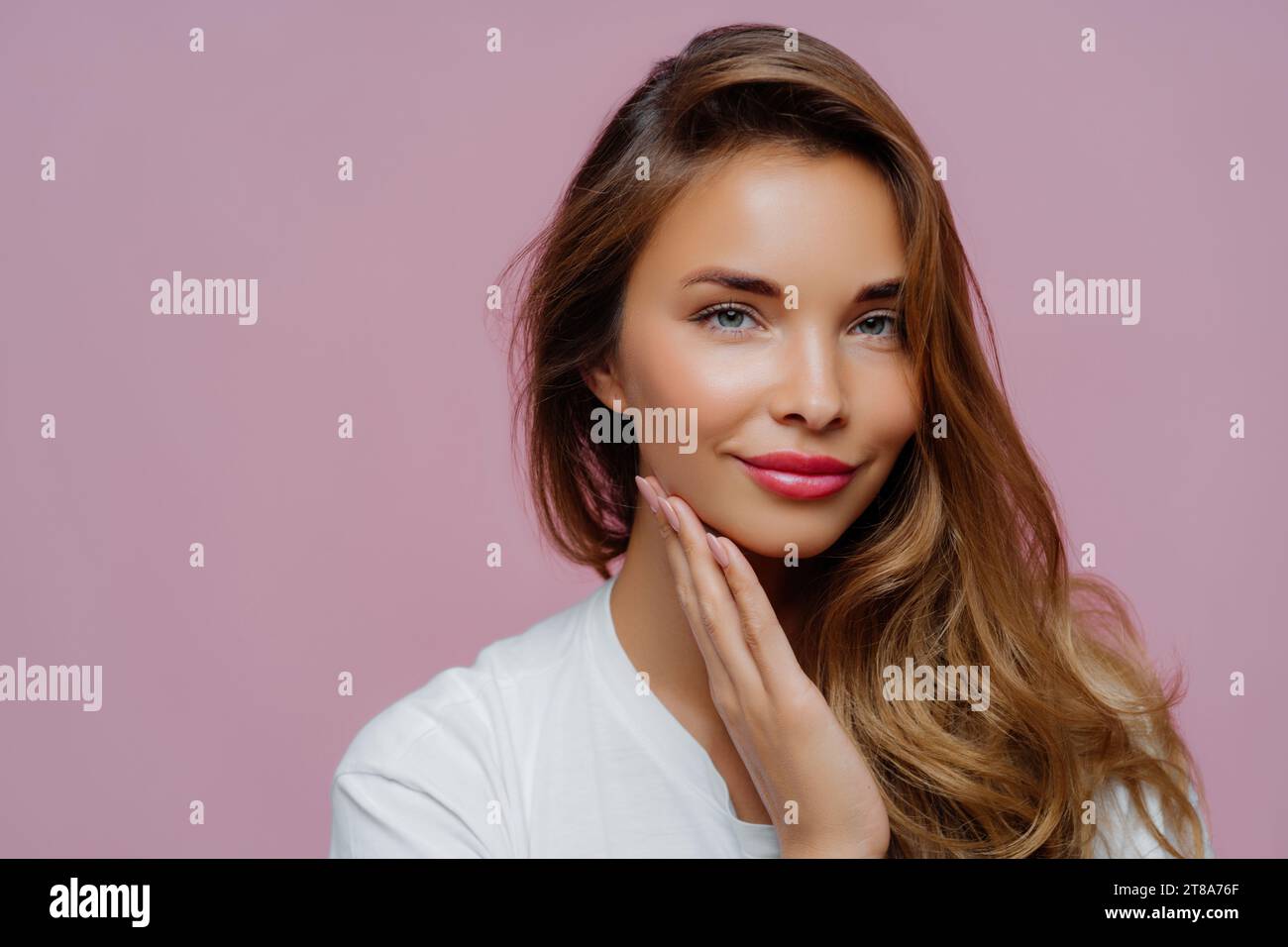 Radiant beauty with hand on cheek and glossy hair, wearing a white ...