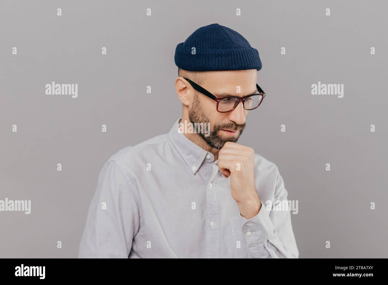 Indoor shot of concentrated man holds chin and focused down, being in ...