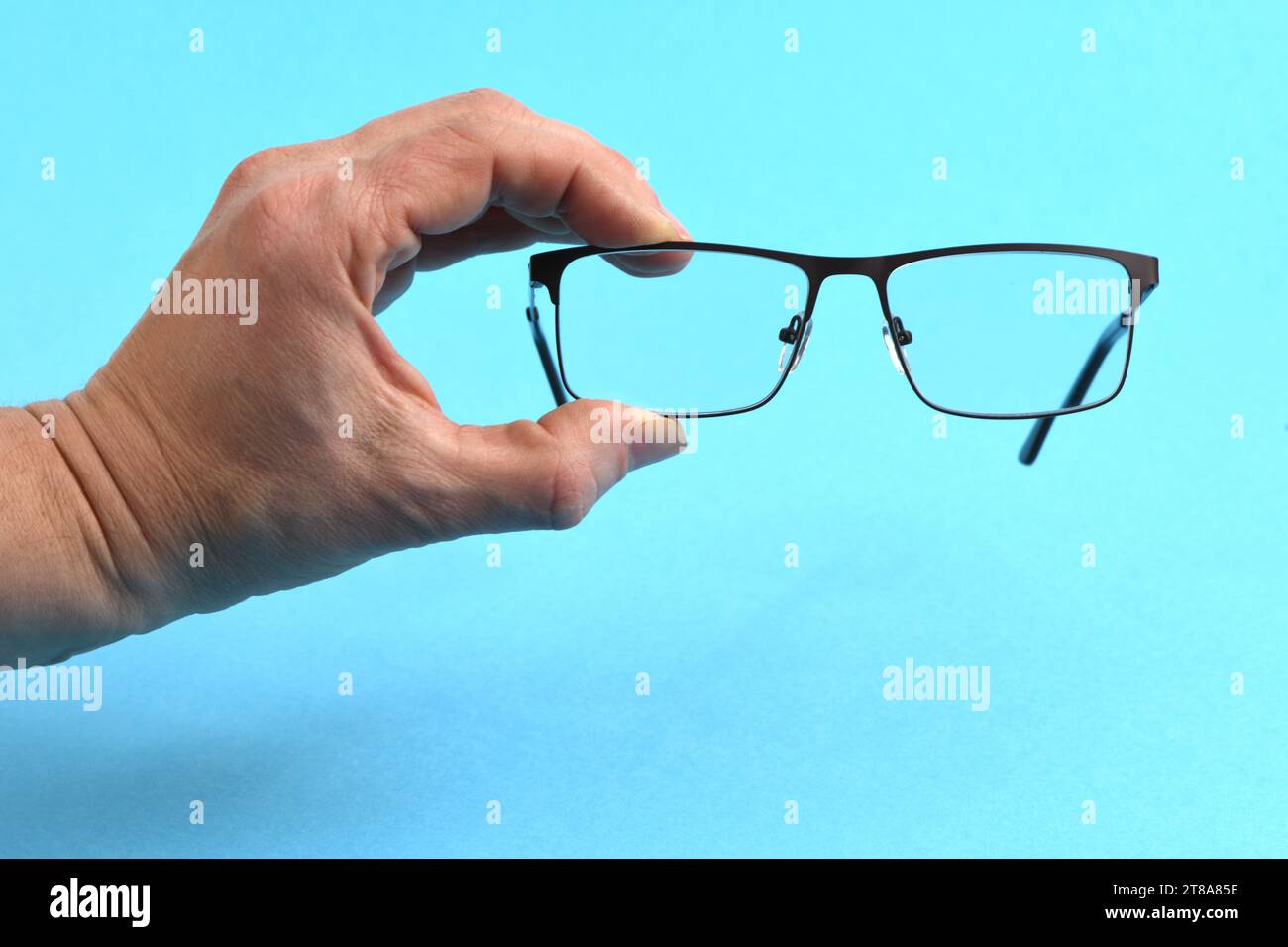 Hand holding plastic black glasses, isolated on blue background. High ...