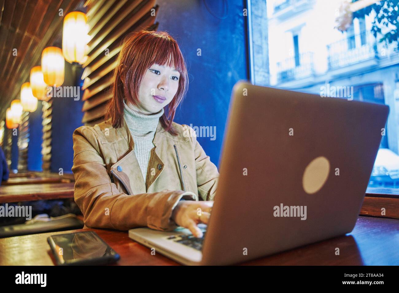 young asian girl in a chinese restaurant using her laptop computer ...