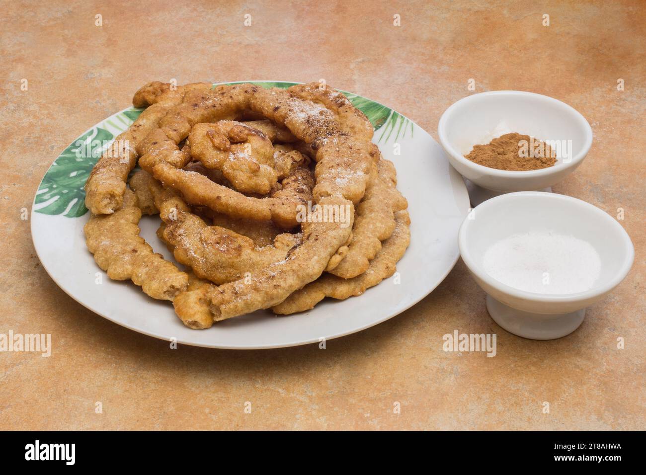 A plate of fried dough twists with two small bowls of powdered ...