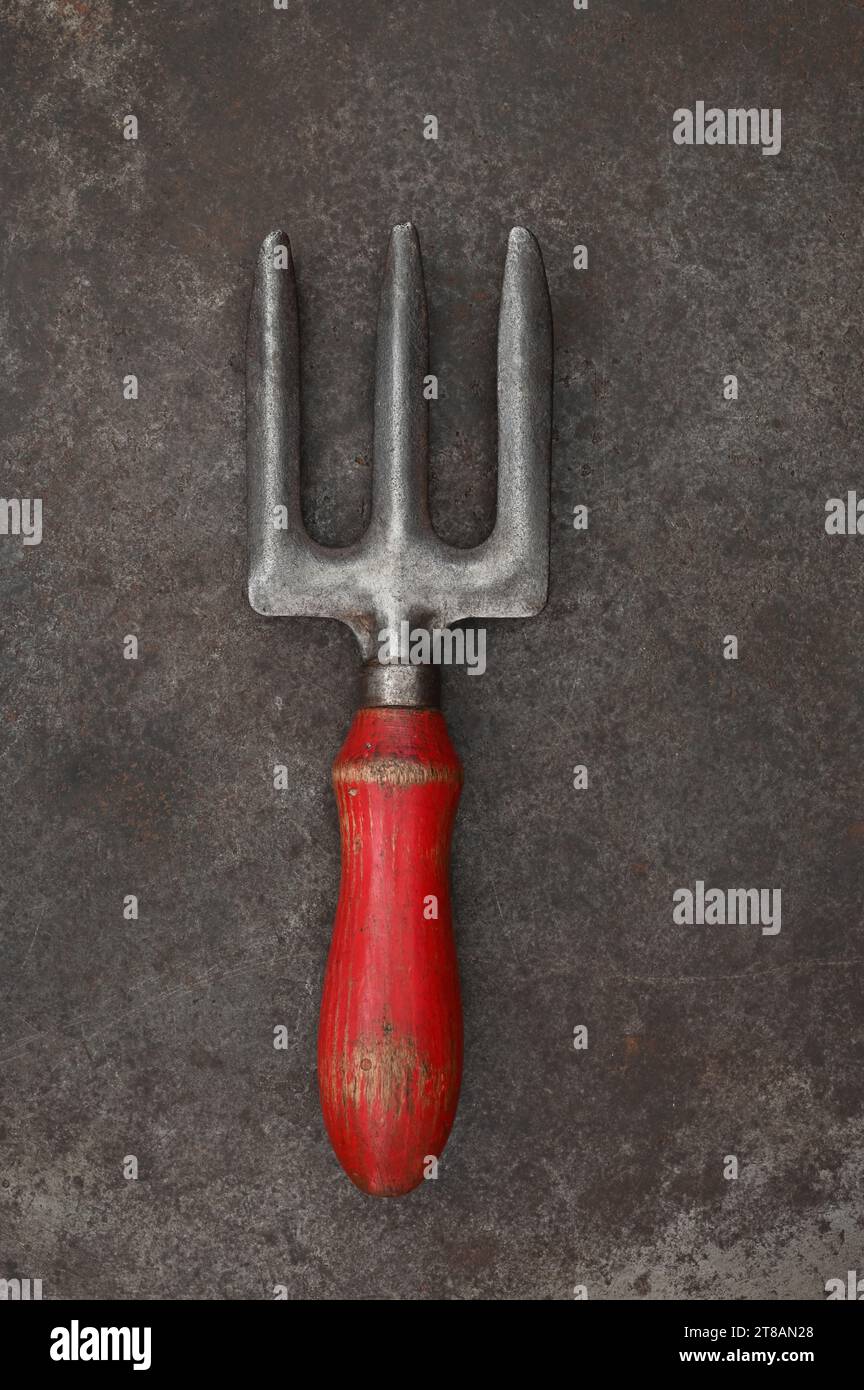 Used and worn garden hand fork with red wooden handle lying on ...