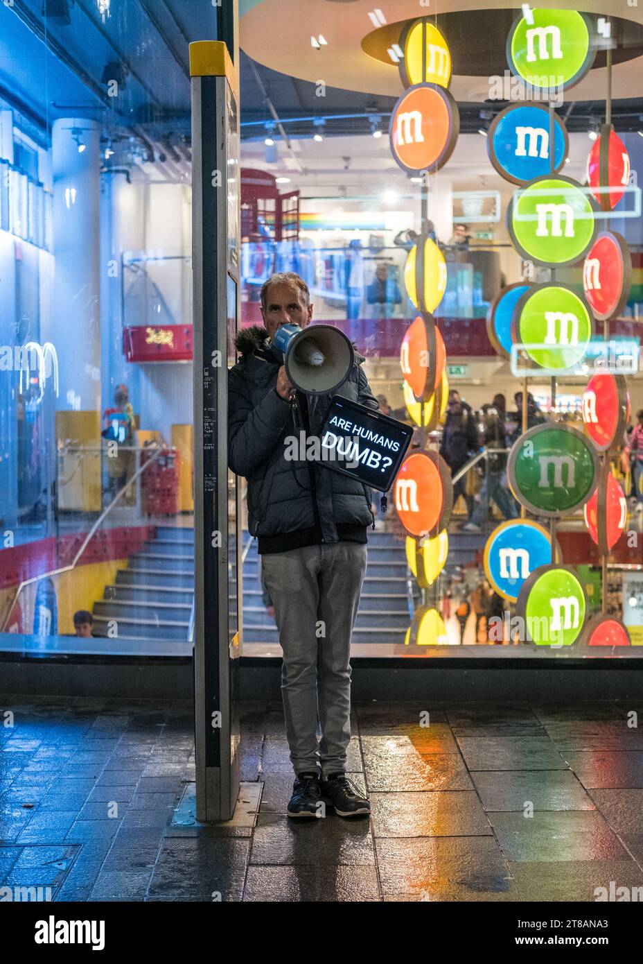 Man with megaphone stands in Leicester Square holding a sign saying ...