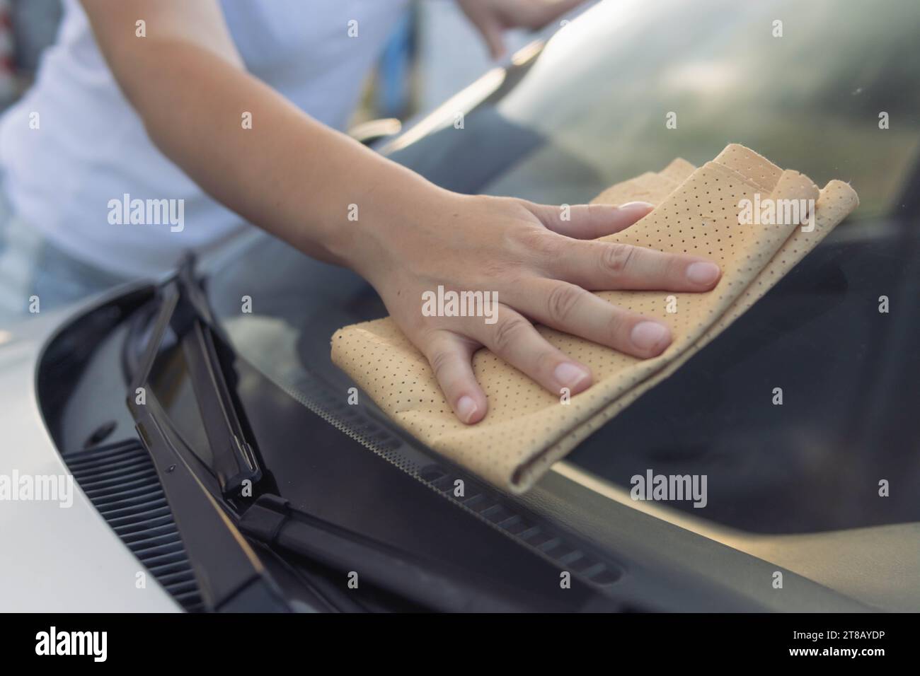 A girl in a white t-shirt wipes the window in the car with a yellow ...