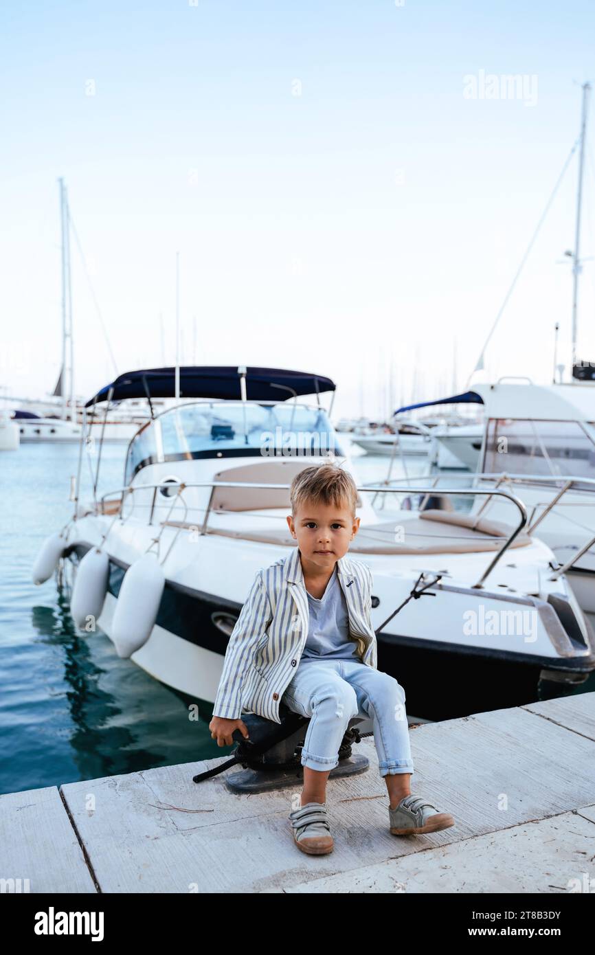 Cute stylish boy sitting on the pier near yacht in marina Stock Photo ...